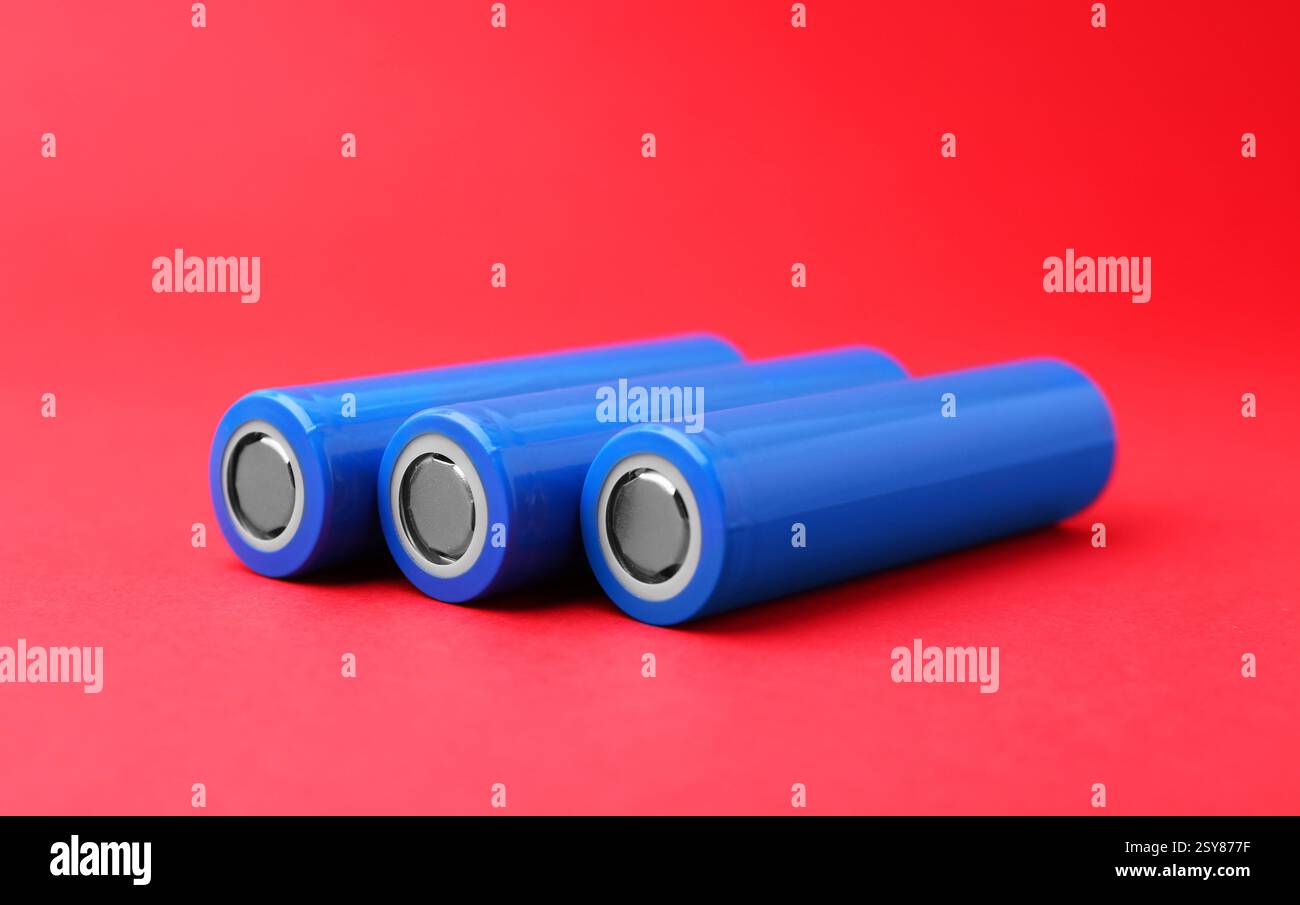 Three AA cell batteries on red background, closeup. Space for text ...