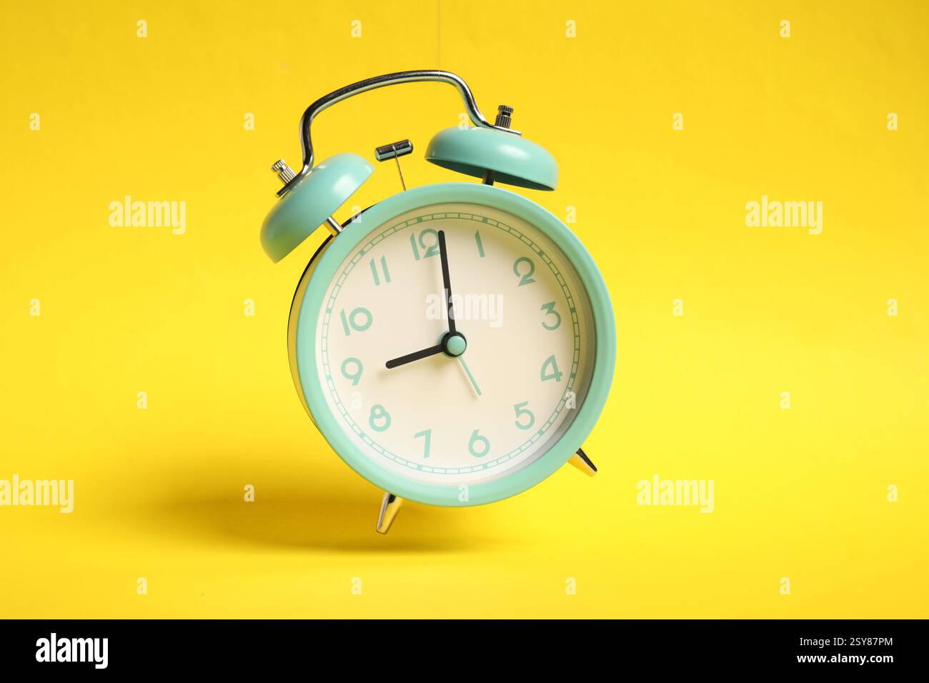 Turquoise alarm clock in air on yellow background Stock Photo - Alamy