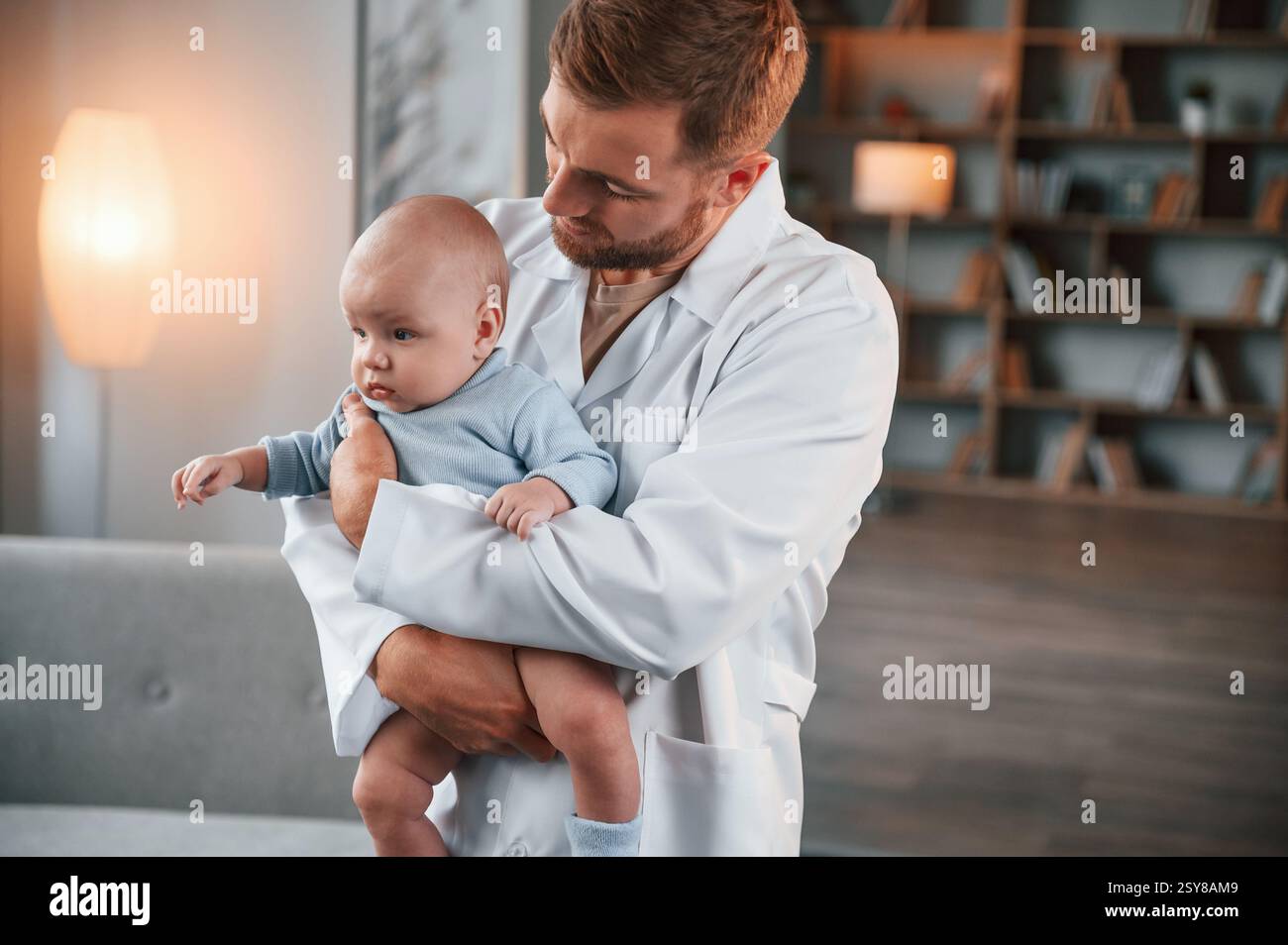 Looking at the kid. Doctor standing and holding newborn baby in hands ...