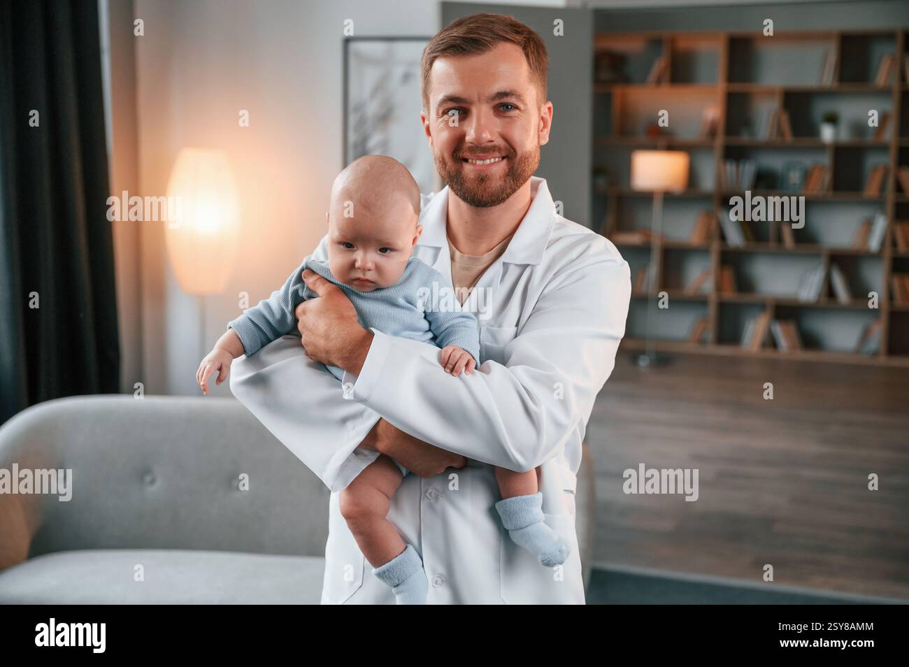 Positive doctor standing and holding newborn baby in hands indoors at ...