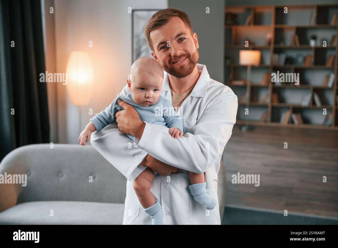 Positive doctor standing and holding newborn baby in hands indoors at ...