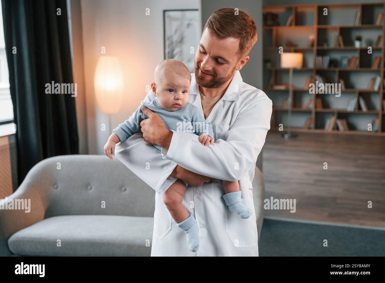 Doctor standing and holding newborn baby in hands indoors at apartment ...