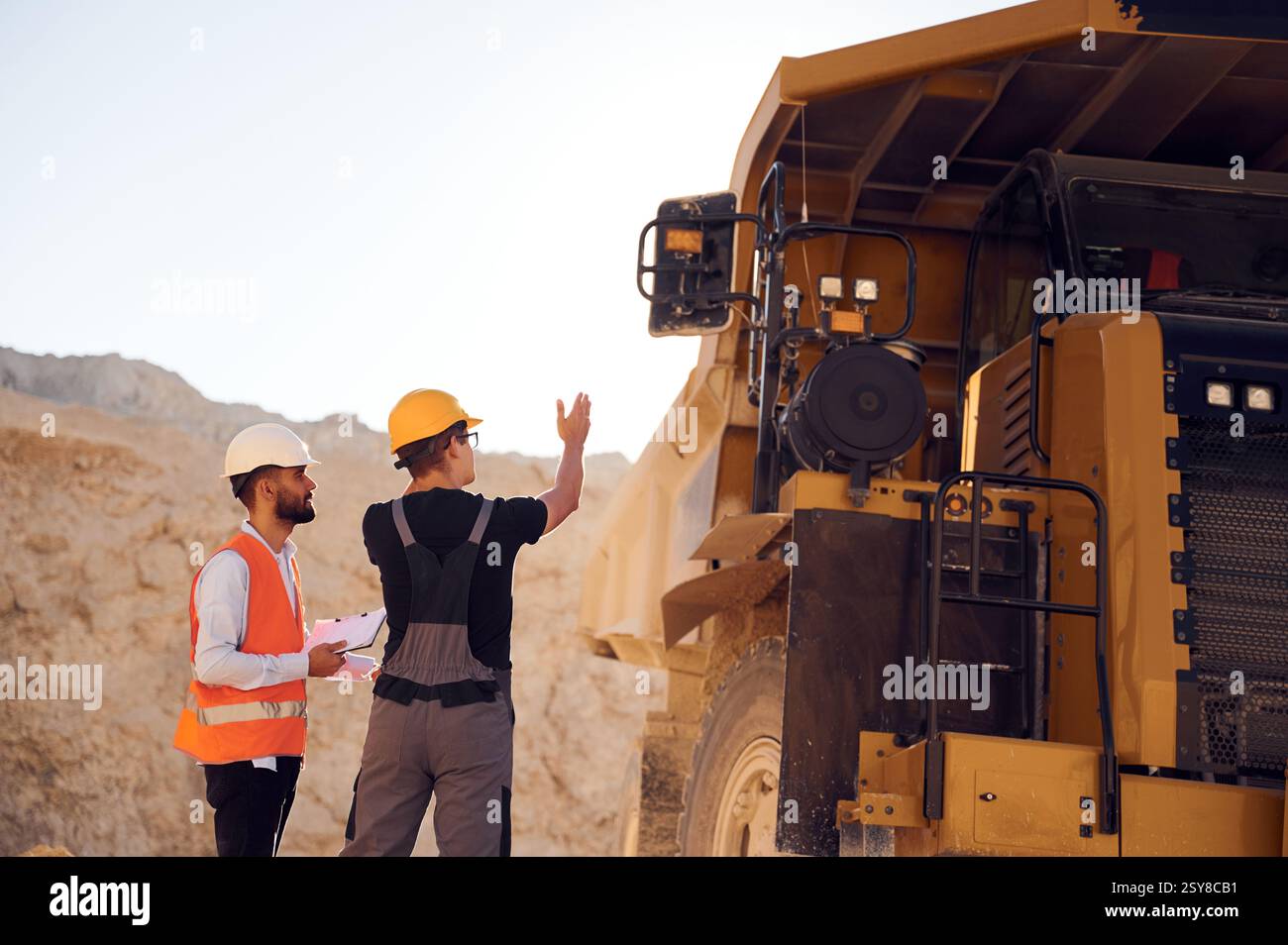 Looking at big haul truck. Two men in uniform are working together in ...