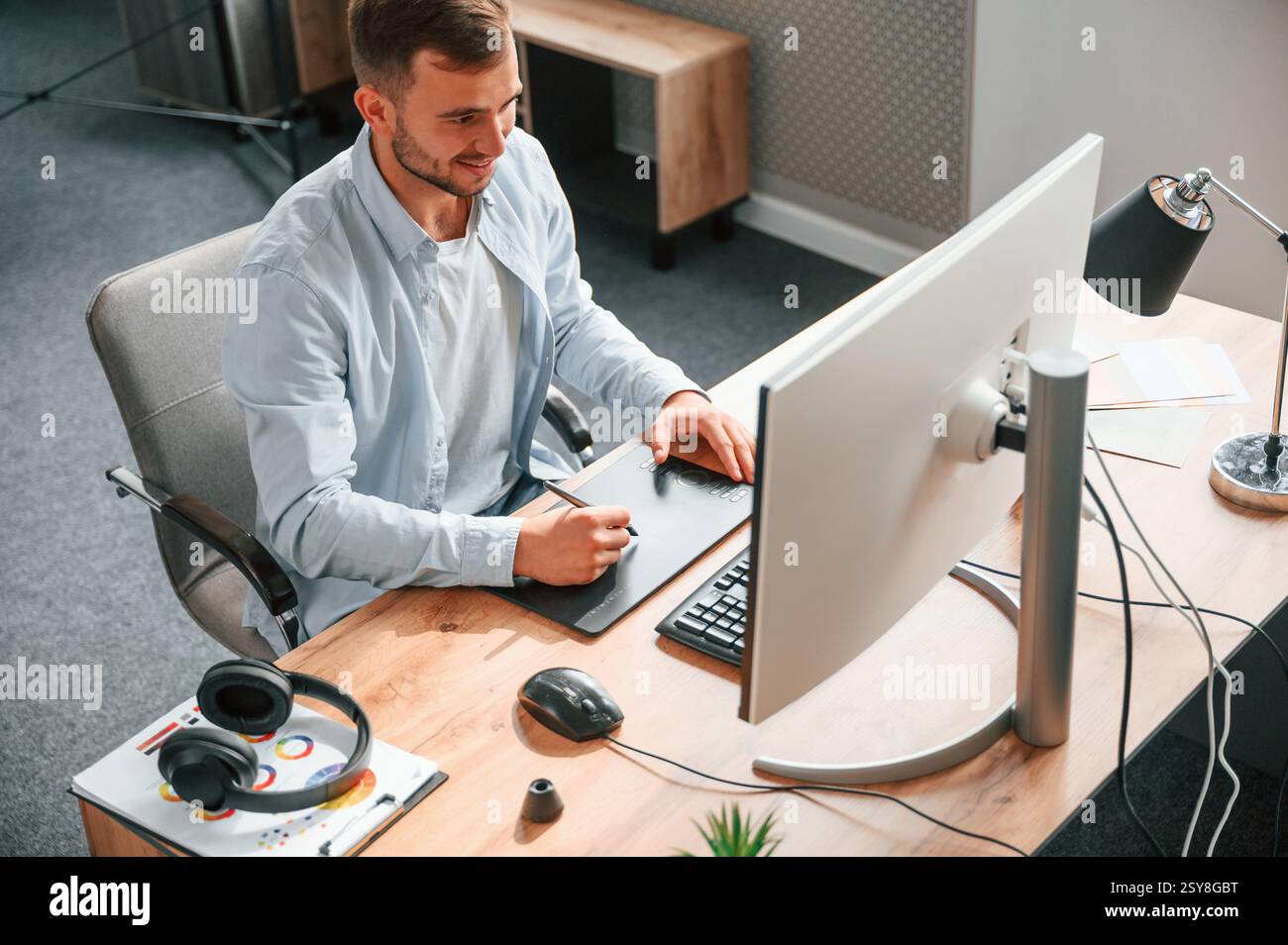 Top view. Designer is sitting by the computer and using graphics tablet ...