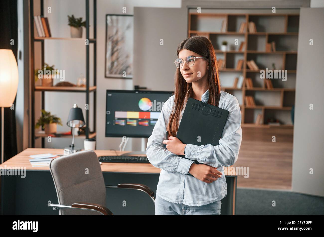 With black colored notepad. Standing and posing. Young female designer ...