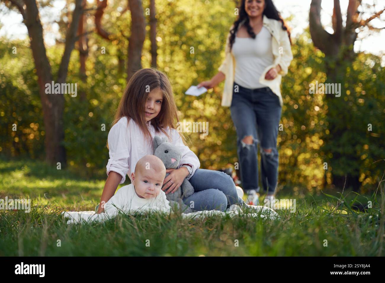 Kid is sitting with her little brother on the ground with mother behind ...