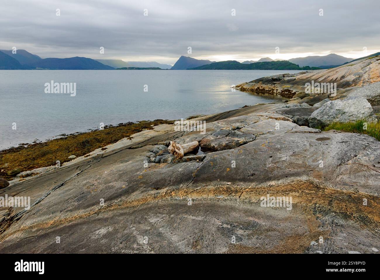 Calm waters reflect the overcast sky as rocky shores line a tranquil ...