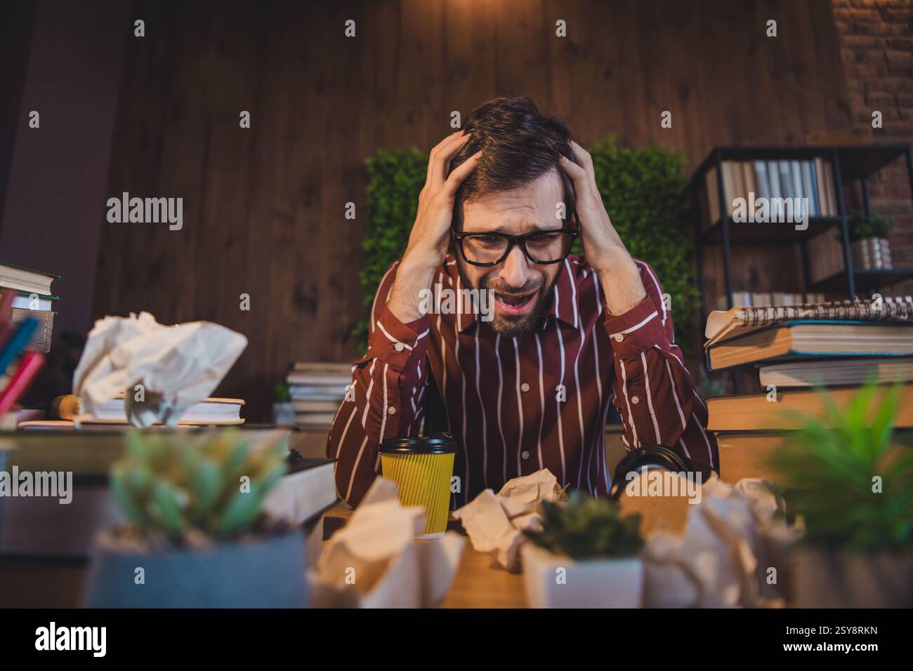 Stressed young man overwhelmed with work and studies in a cozy home ...