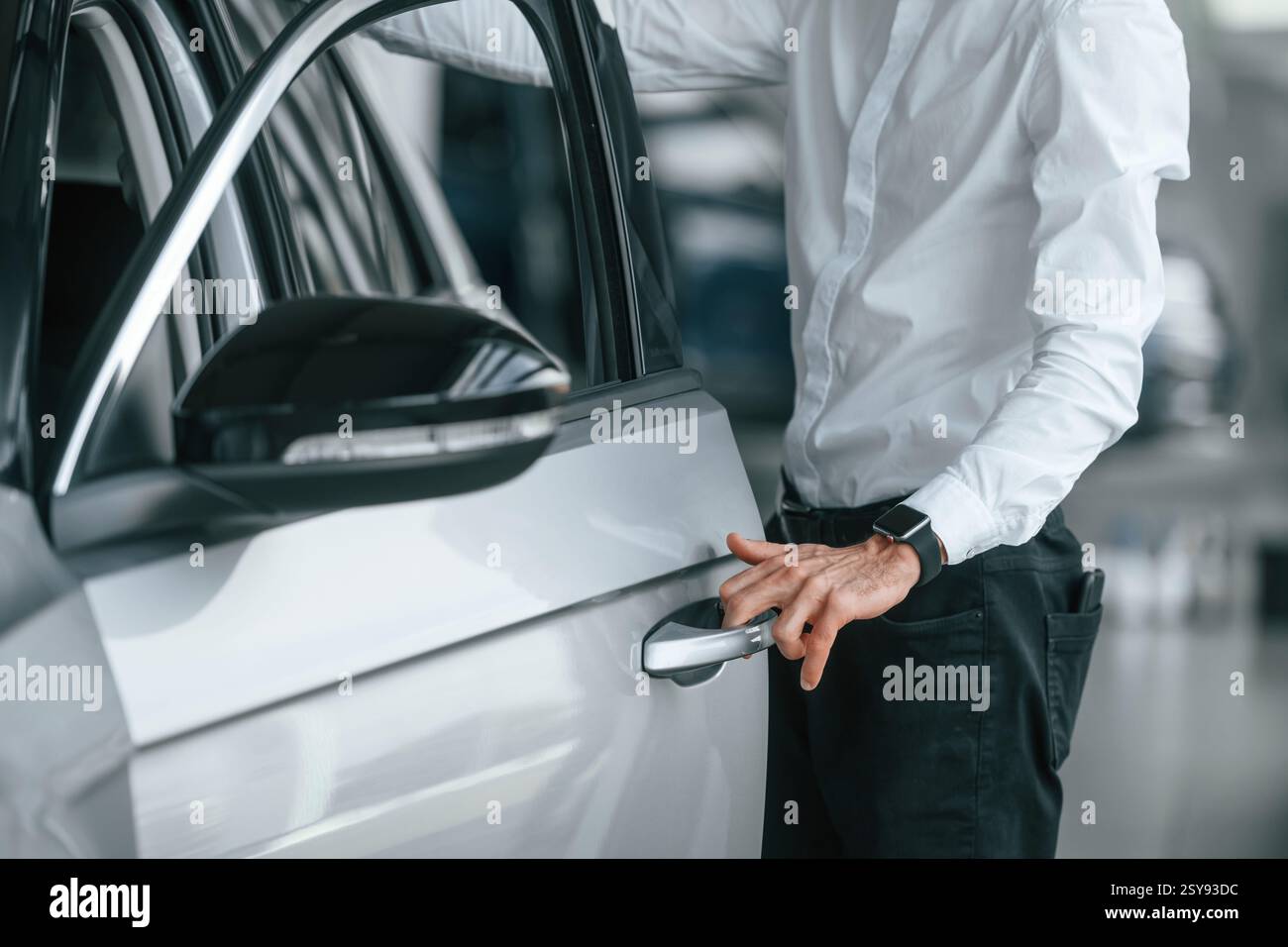 Opening the door. Young man in white clothes is in the car dealership Stock Photo - Alamy