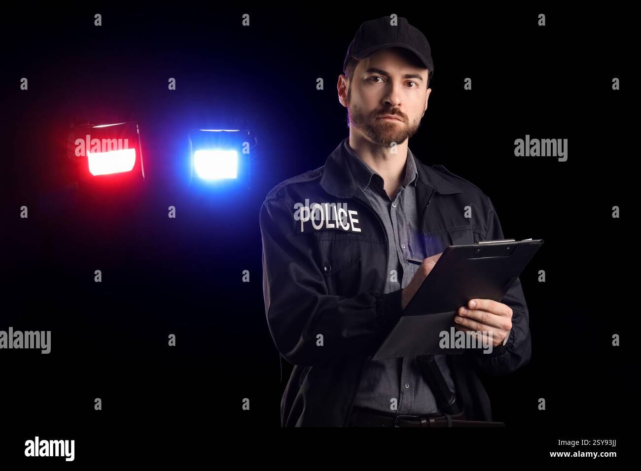 Male police officer writing in clipboard against flashing siren lights ...
