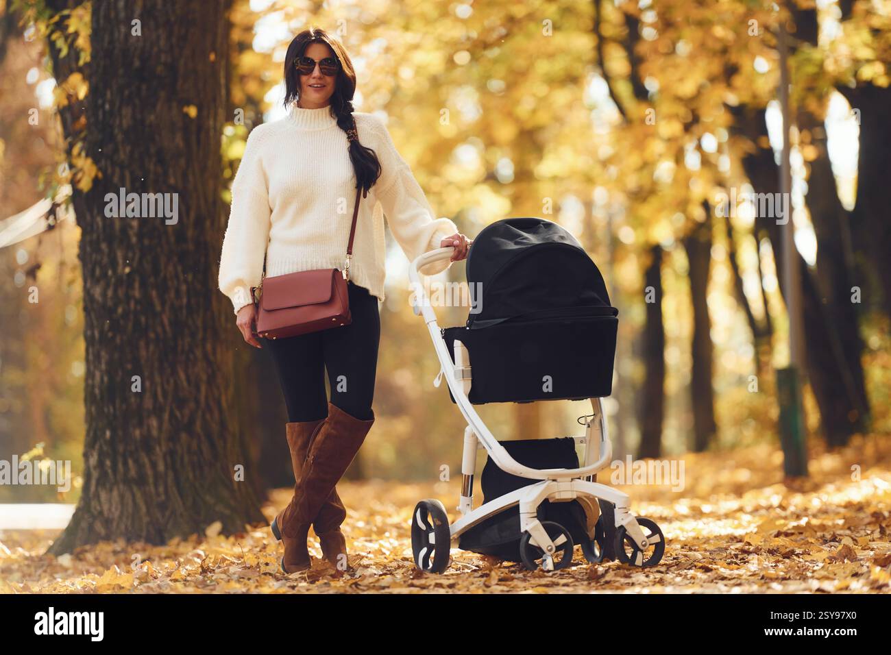 Mother with black colored pram is having a walk in forest at daytime ...