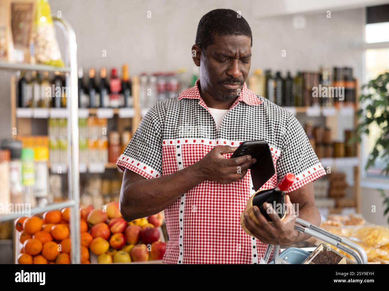 African man customer at shop scans QR code on wine bottle using phone ...