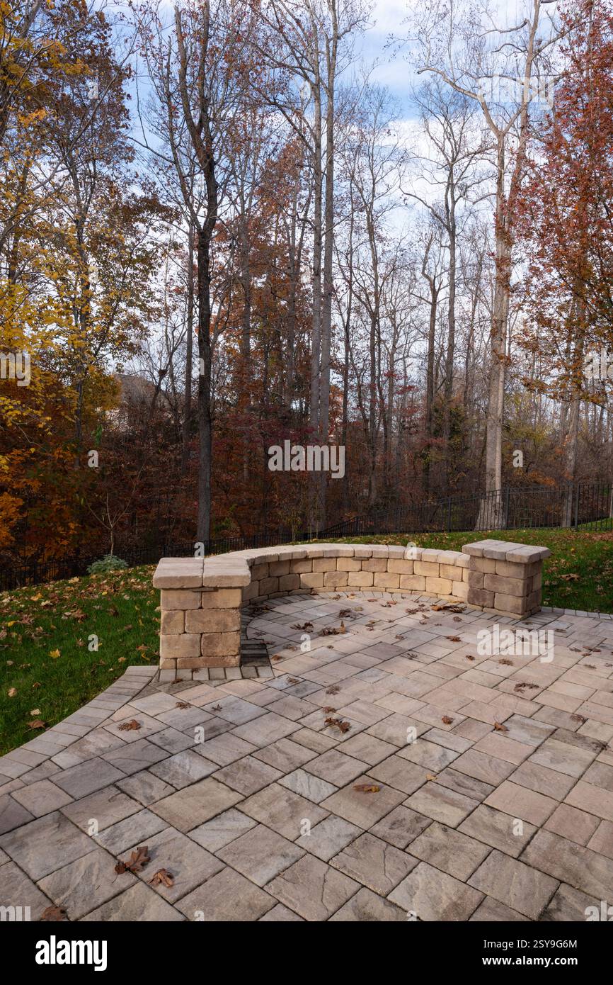 A serene backyard patio with a curved stone wall, surrounded by fall ...