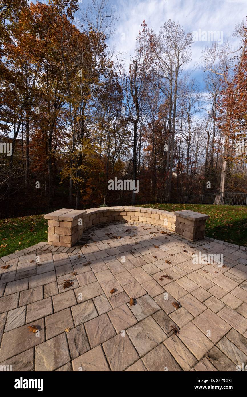 A serene backyard patio with a curved stone wall, surrounded by fall ...