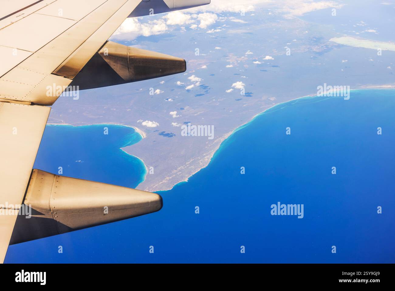 Aerial view of airplane wing over Caribbean Sea coastline with blue ...