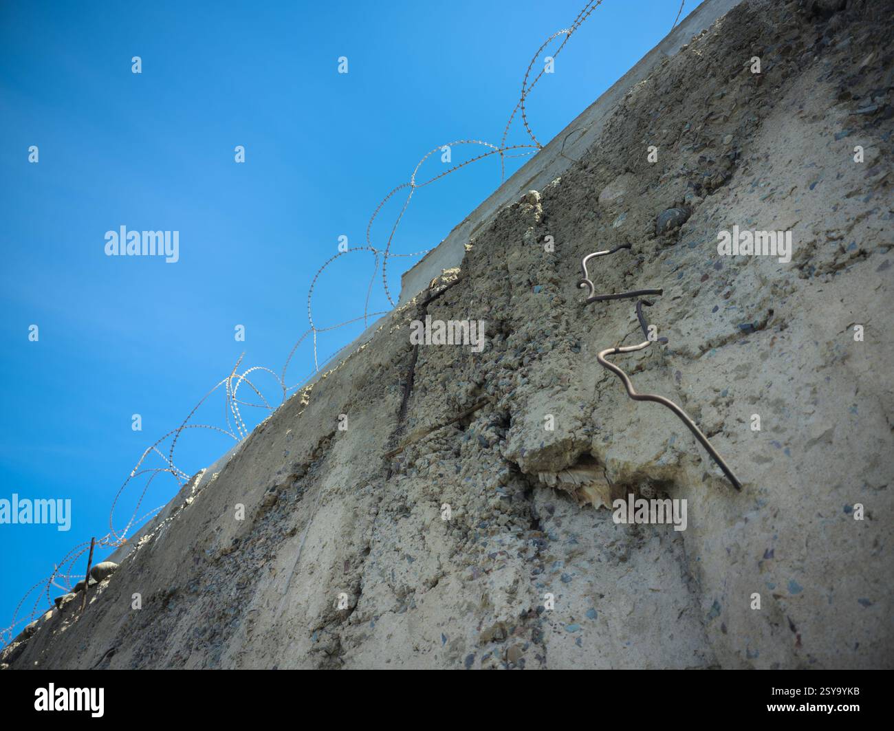 old decayed concrete wall with barbwire on top with blue sky above ...