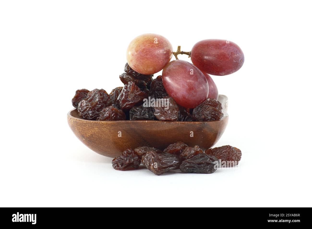 A wooden bowl overflows with dark, plump raisins, complemented by a ...