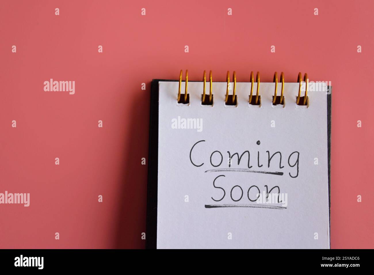 A notepad with the handwritten phrase "Coming Soon" on a bright pink ...