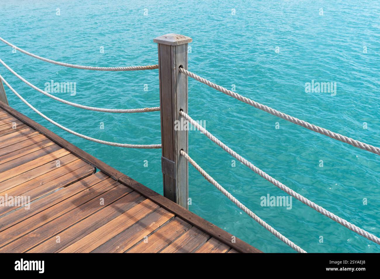 Wooden pier with posts and ropes with sparkling sea water. Wooden pier ...