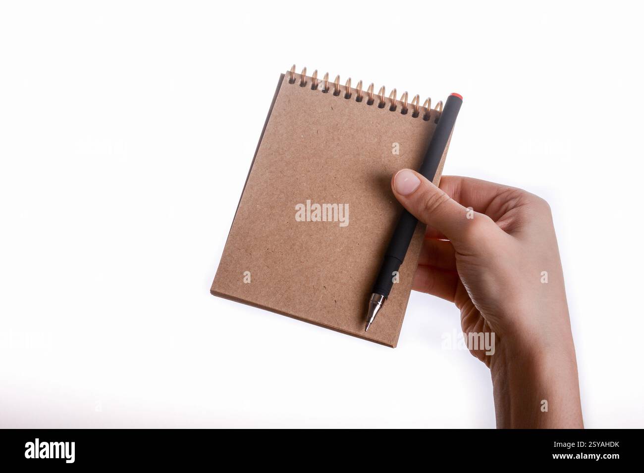 Spiral brown notebook with a pen held by a child on a white background ...