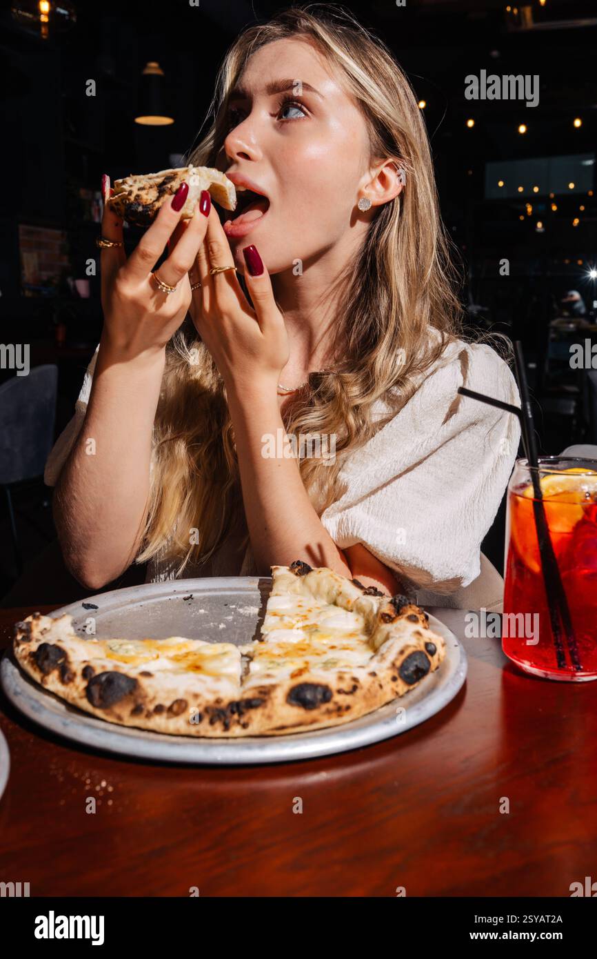 Woman enjoying a slice of creamy Four Cheese pizza paired with a berry lemonade at a stylish ...