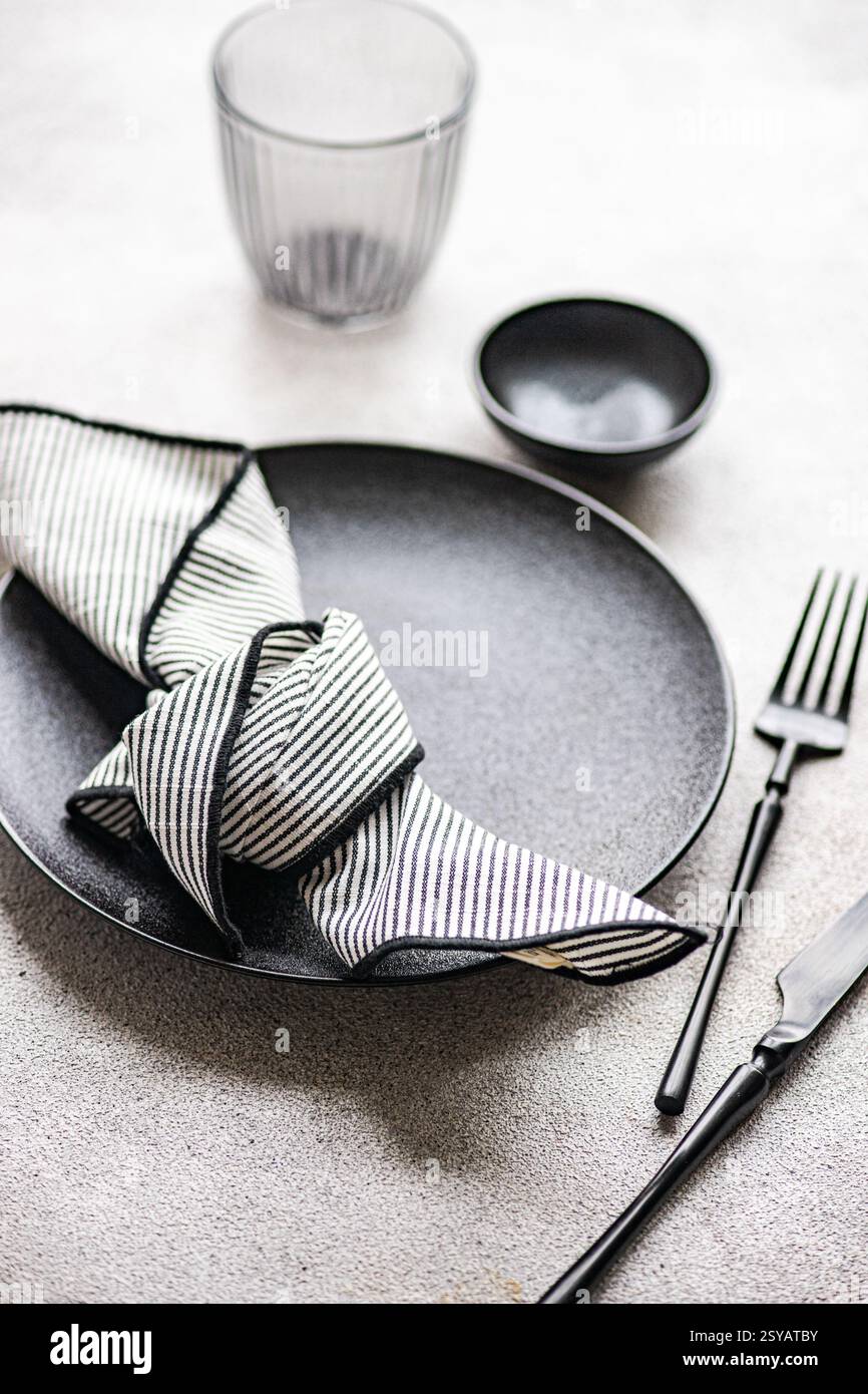 A stylish table setting featuring a black plate, black cutlery, and a ...