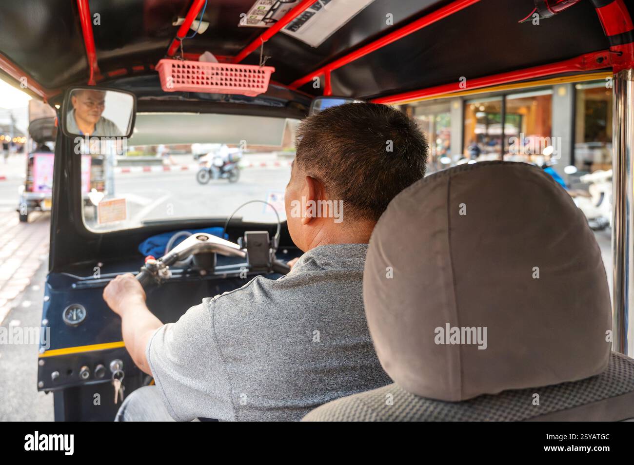 Back view of an unrecognizable male Thai tuk tuk driver is captured ...