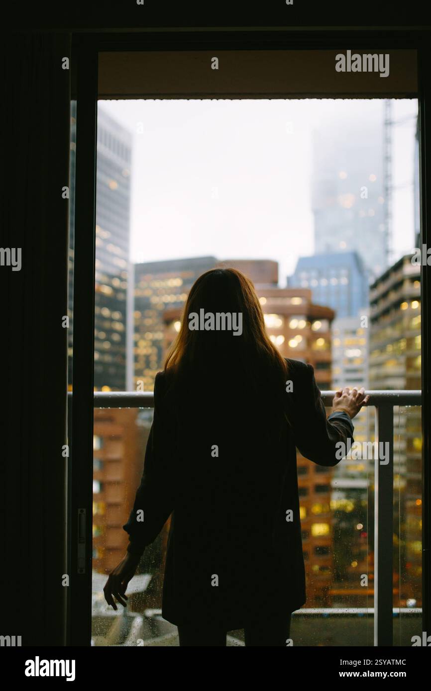 Back view of unrecognizable redhead woman standing by a window in a ...