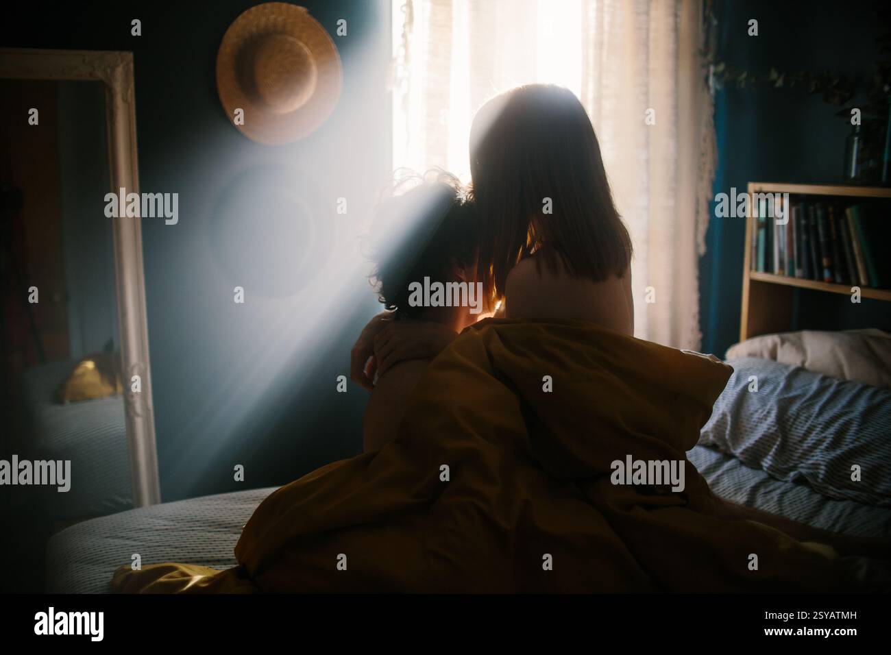 A couple shares an intimate embrace on a bed, bathed in warm morning ...