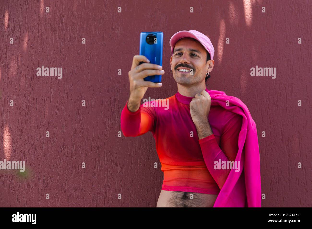A young Spanish Caucasian man with a mustache, wearing vibrant pink ...
