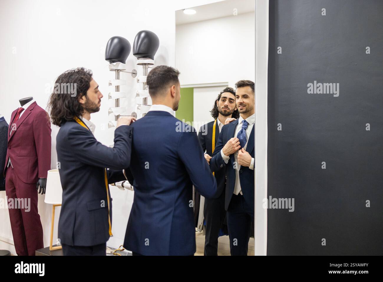 A tailor adjusts a client suit in front of a mirror, ensuring an ...