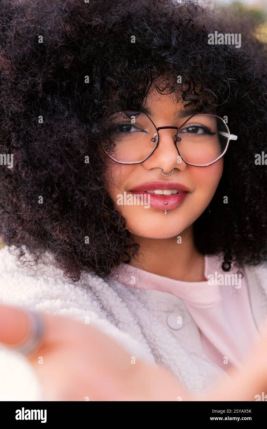 A young latin woman with voluminous curly hair, wearing round glasses ...