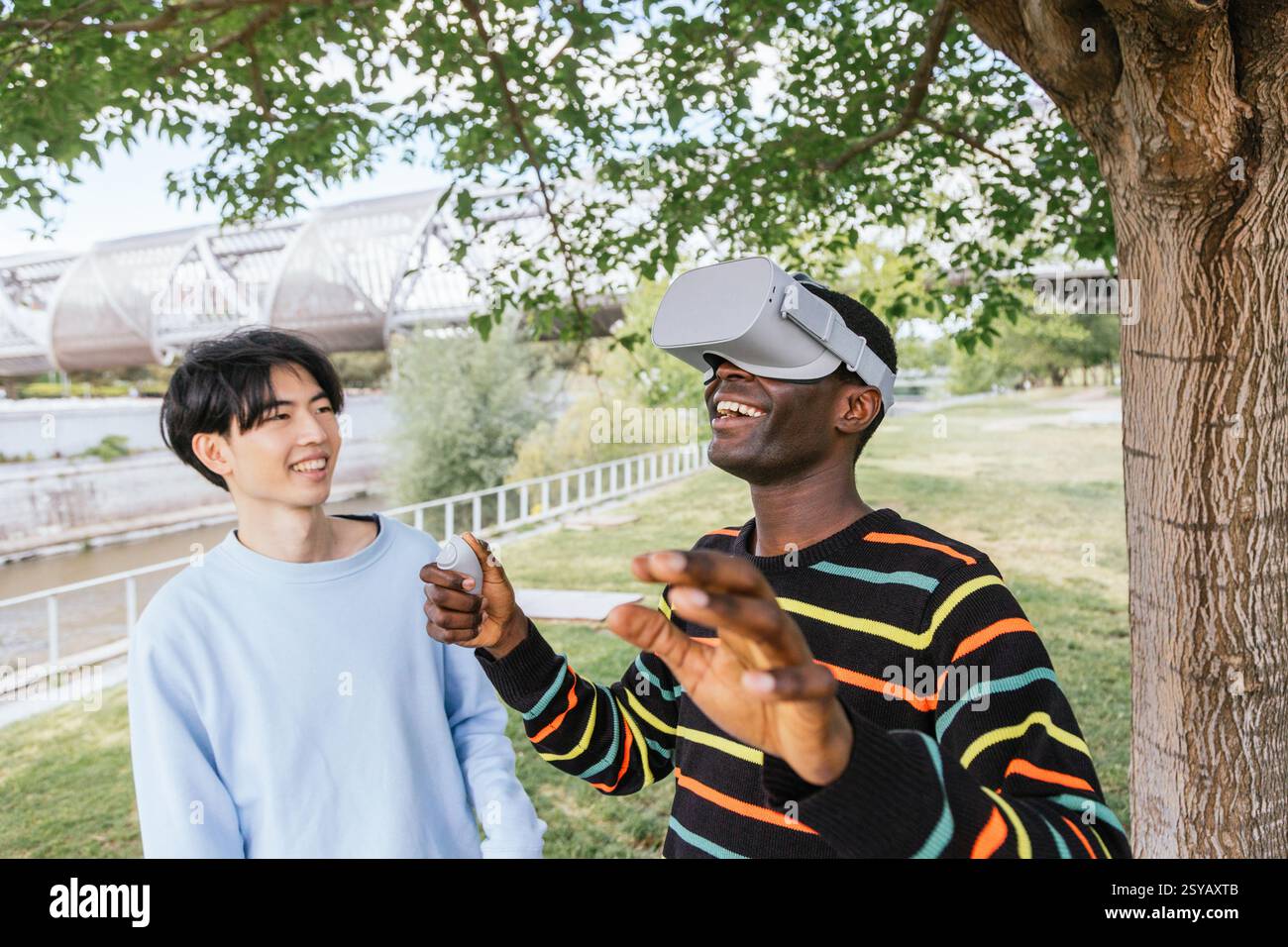 Two friends enjoy a VR experience outdoors. One wears a VR headset ...