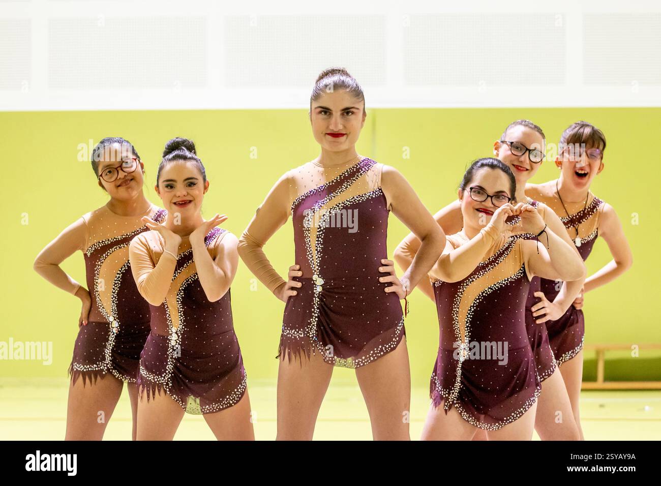 A diverse group of rhythmic gymnasts in sparkling outfits strike joyful poses. Their expressions ...