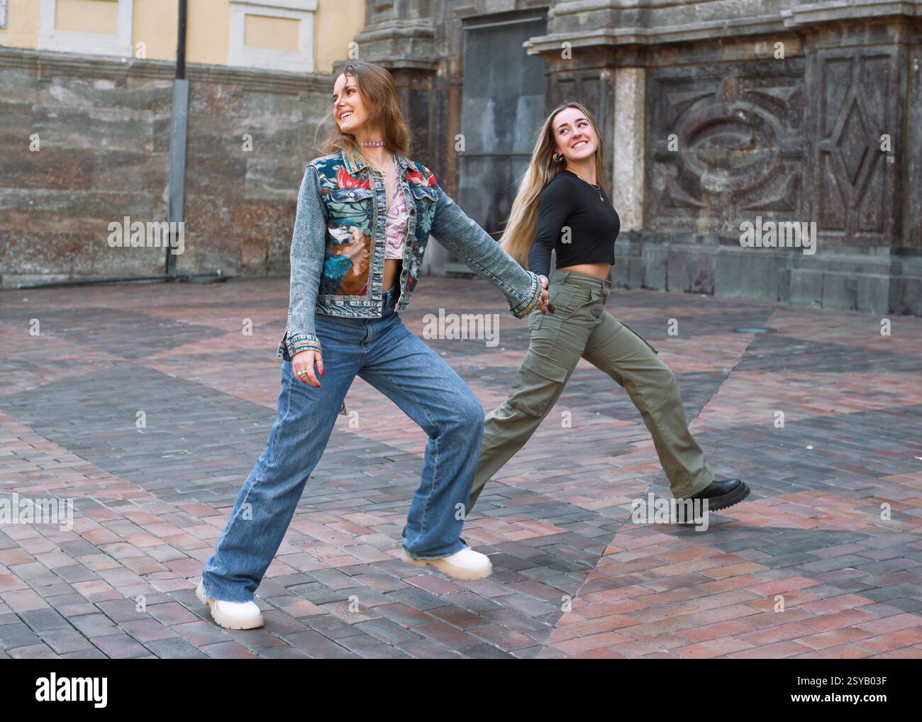 Two young woman friends energetically walk hand in hand across a brick ...