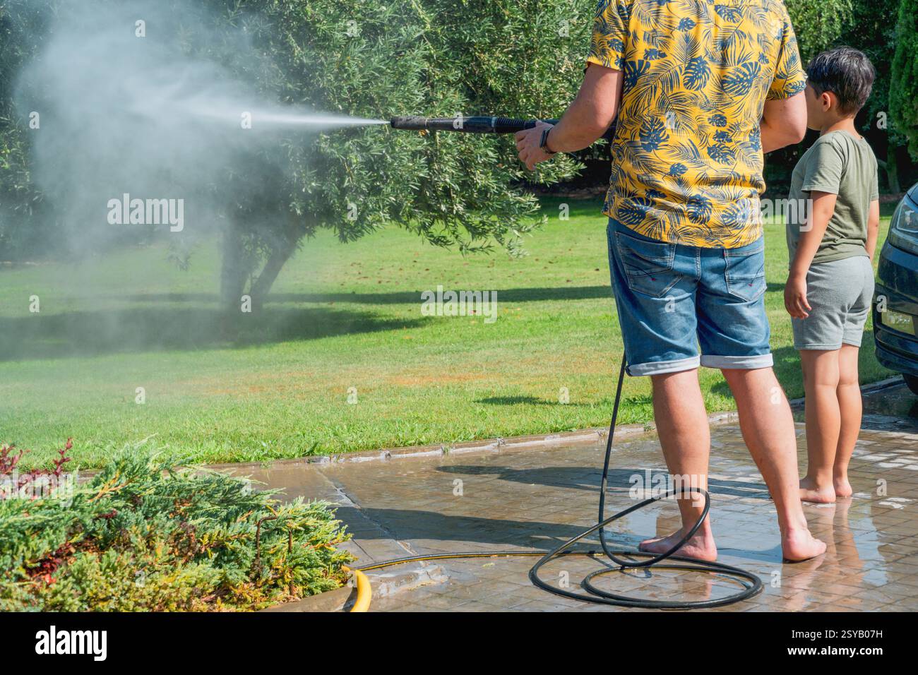 A father and child clean the garden with a pressure washer in summer ...