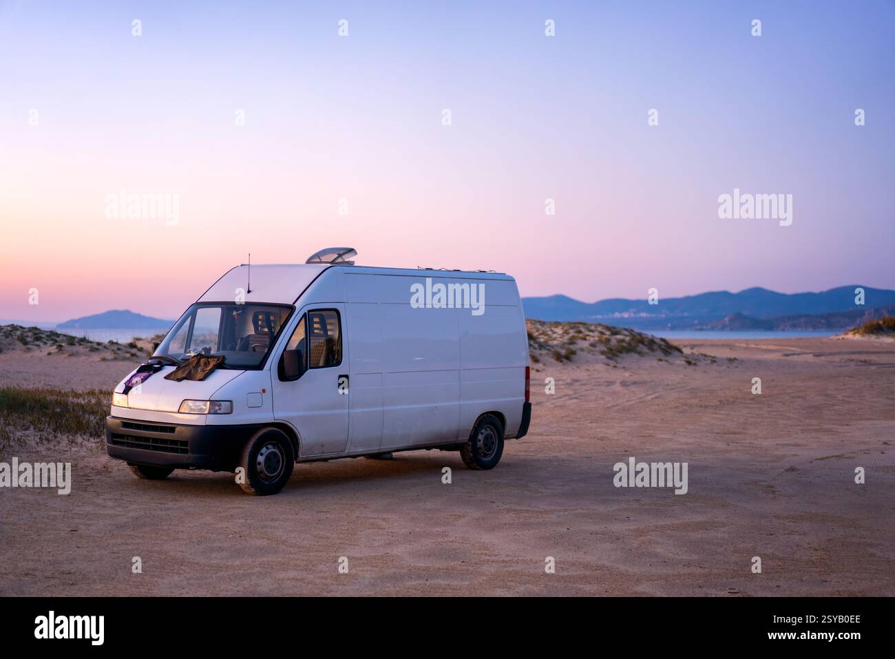 A white camper van parked on a sandy beach in Greece during sunset. The ...