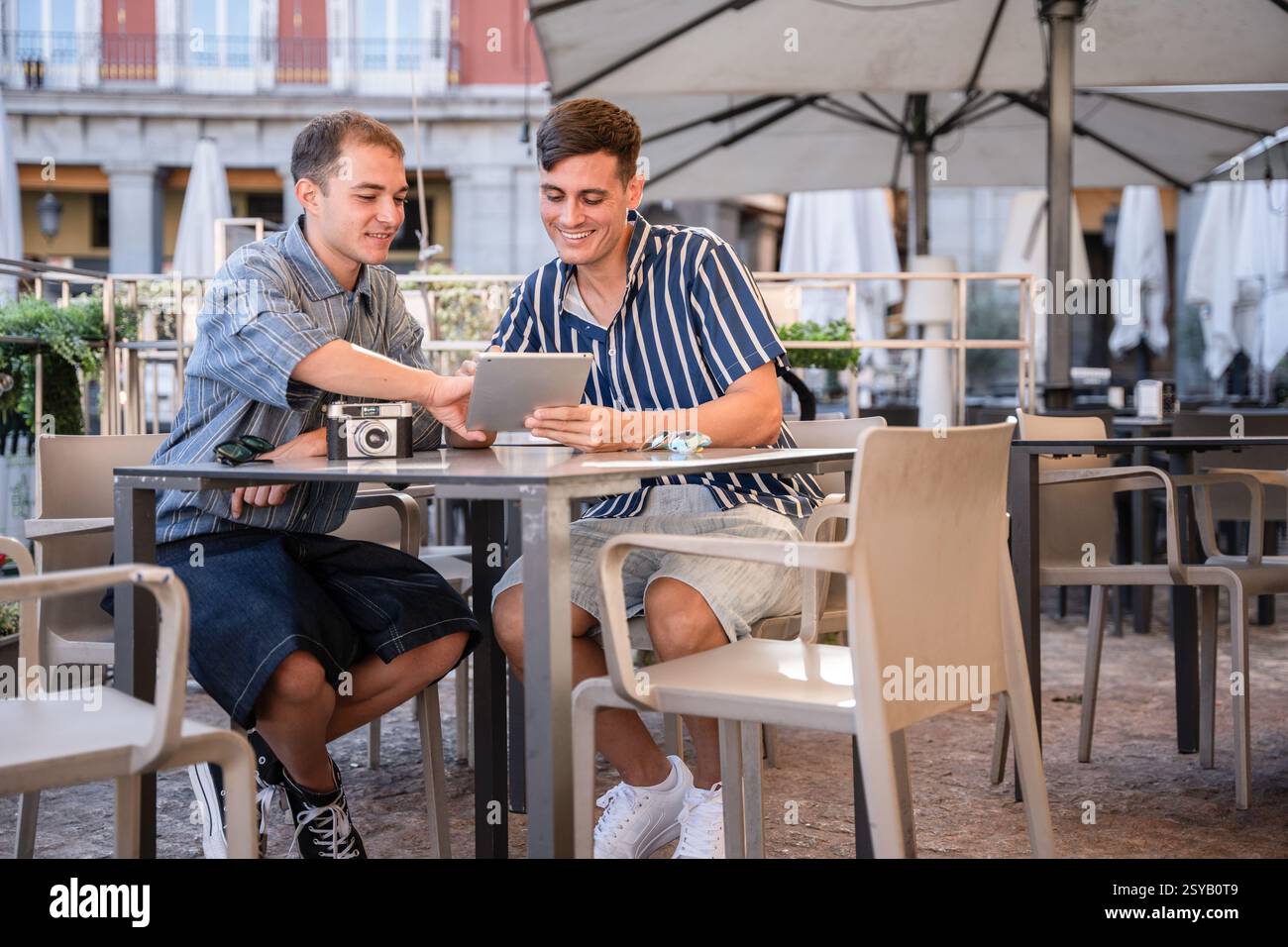 Gay couple sitting at an outdoor cafe in Plaza Mayor, Madrid, smiling ...