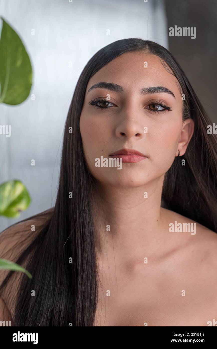 Portrait of a woman with long dark hair and subtle makeup, gazing off ...