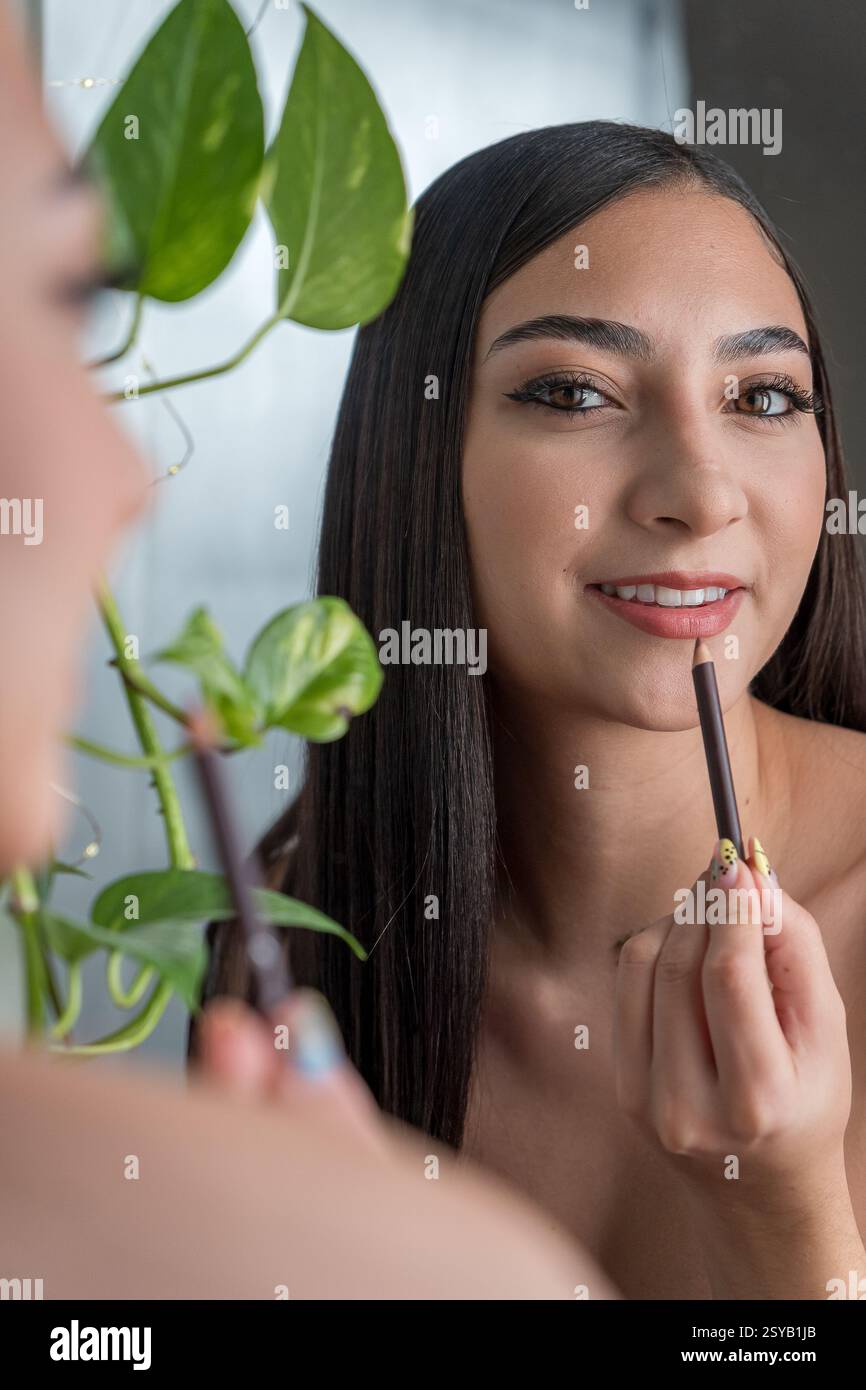 A woman applies lip liner while smiling at her reflection in a mirror ...