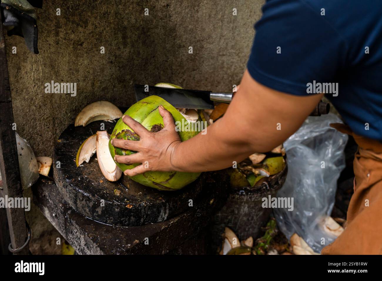 A person uses a sharp knife to skillfully open a coconut on a wooden ...