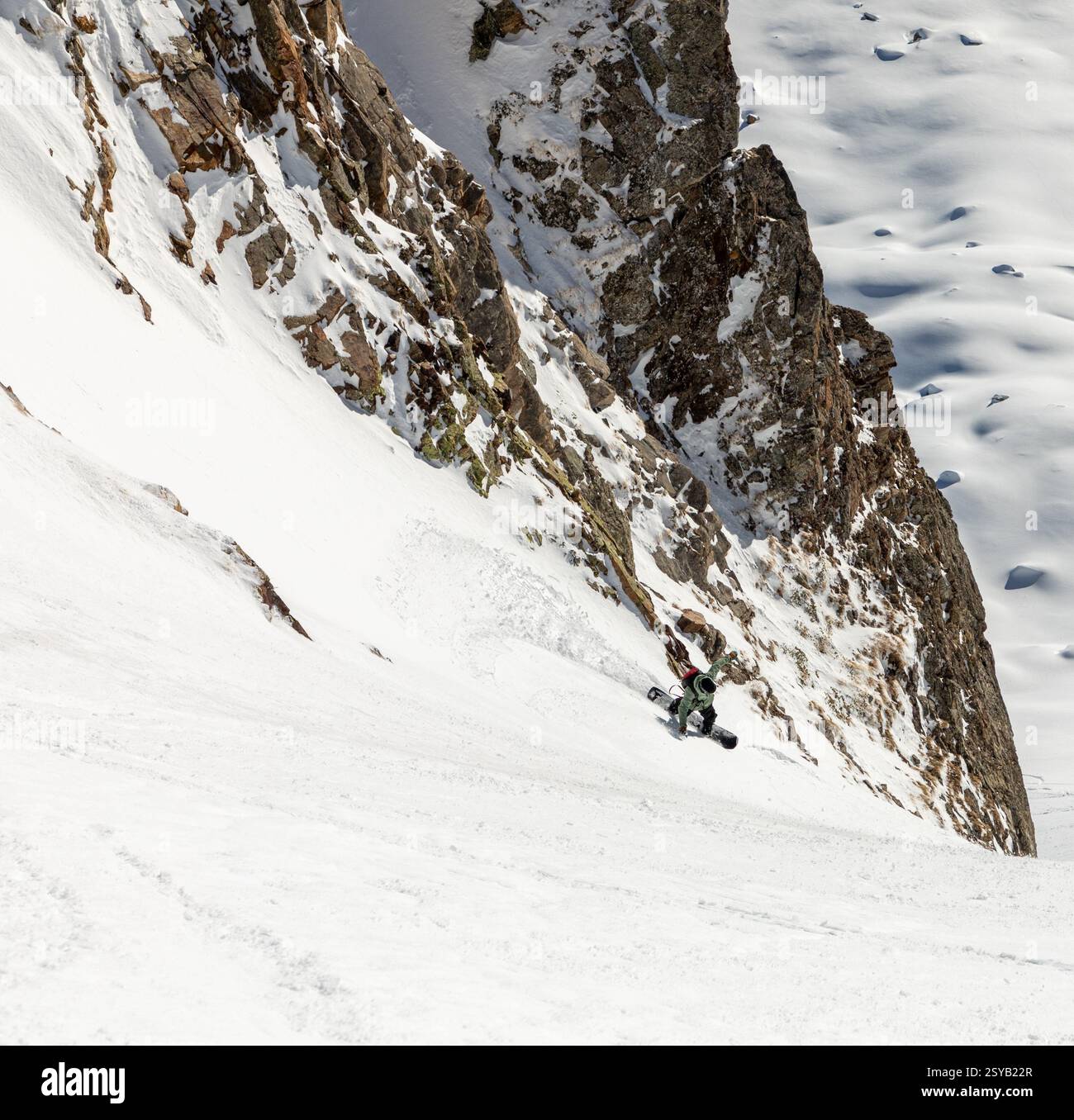 A snowboarder skillfully descends a steep, snowy slope surrounded by ...