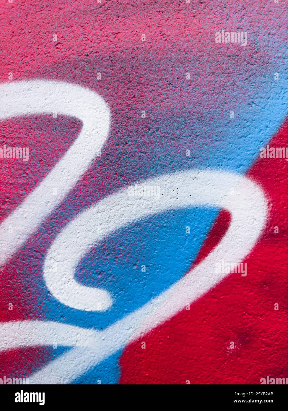 A close-up of vibrant graffiti artwork, showcasing red, blue, and white colors on a textured ...