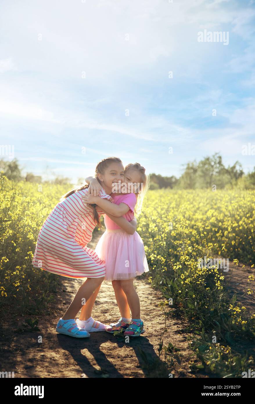 Two young sisters embrace each other with joy in a field of yellow ...