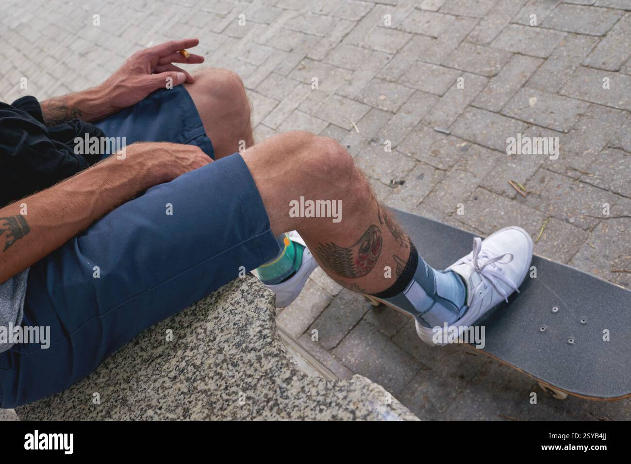 Man, skateboard and legs to relax in city, smoking cigarette and ...