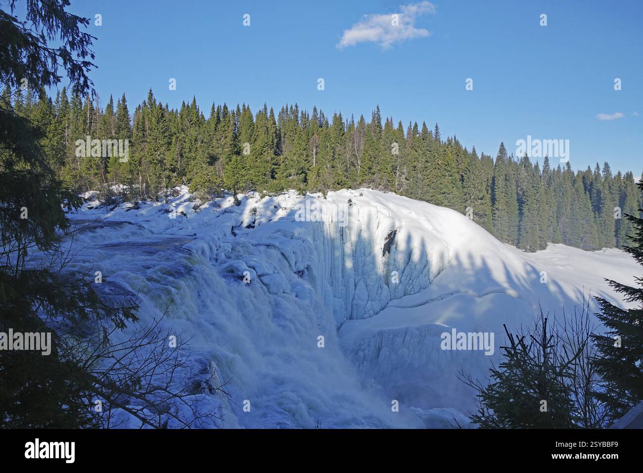 A frozen waterfall in a winter landscape with forest and clear sky ...