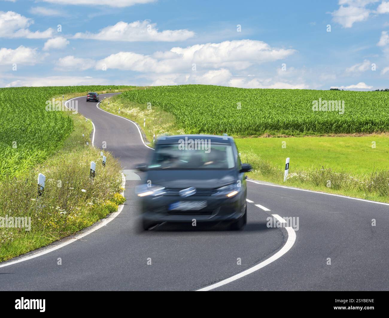 Car driving on winding country road through green fields under blue sky ...