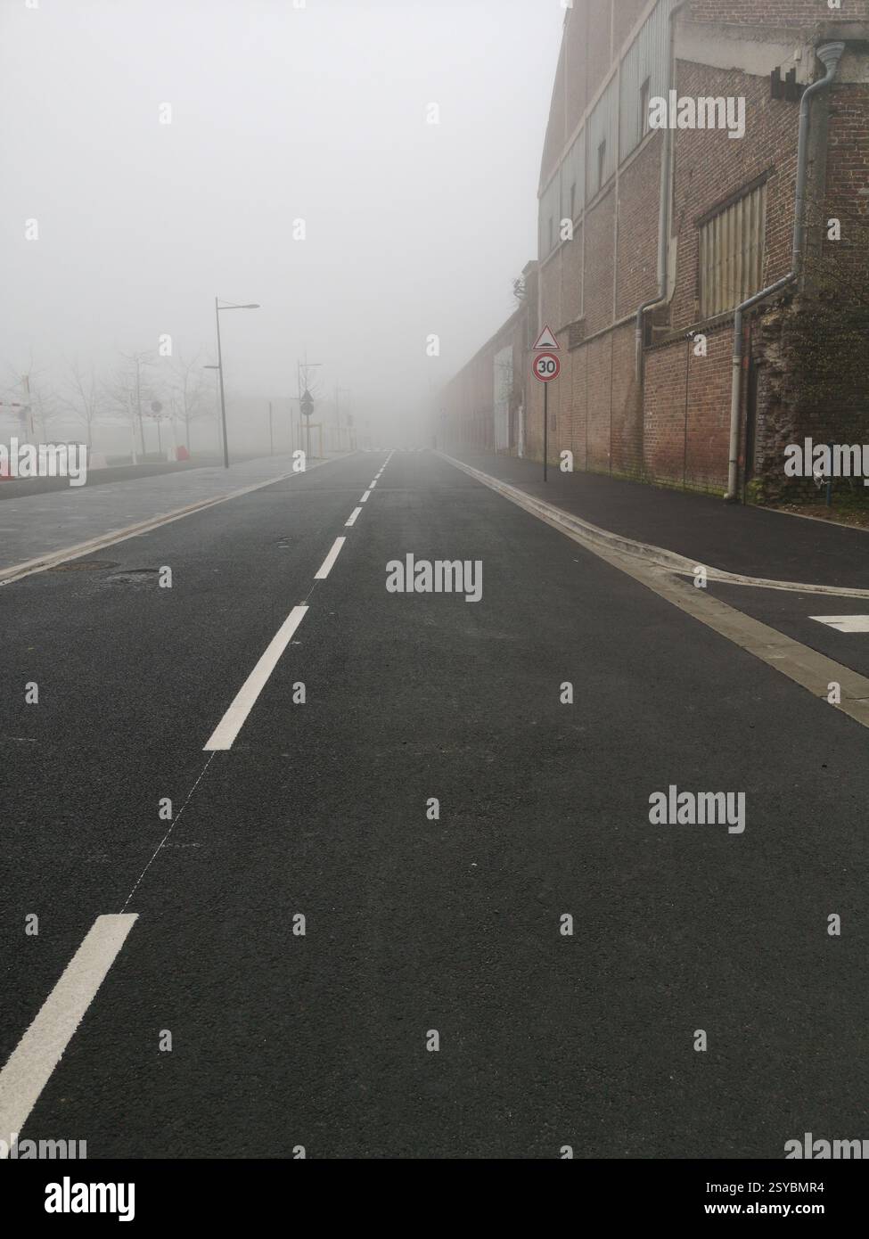 A foggy urban street with a brick building on the right and street ...
