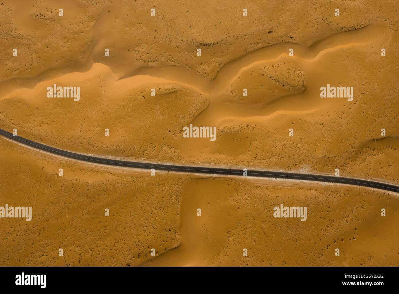 Aerial view of a straight road crossing sand dunes in the Sahara desert ...