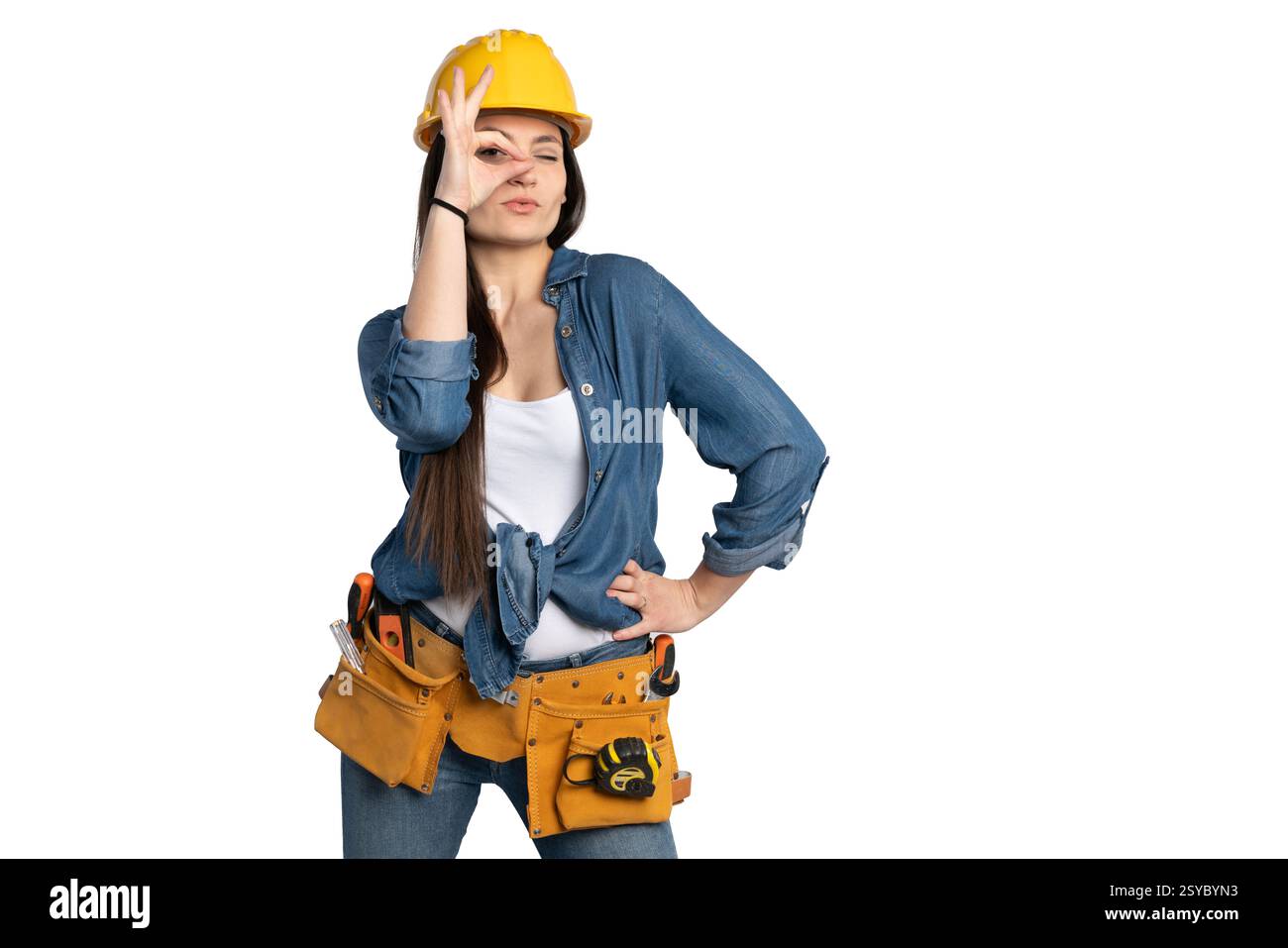 A confident female construction worker wearing a yellow hard hat and denim work attire playfully ...